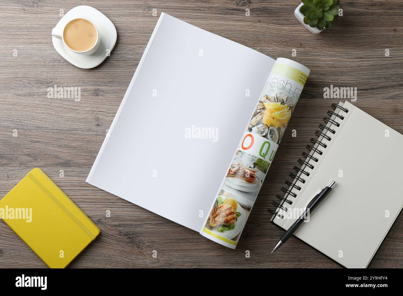 Open magazine with blank page, coffee, plant and stationery on wooden ...