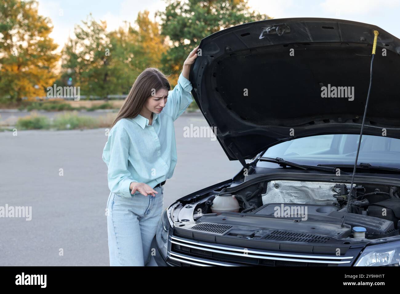 Stressed woman looking under hood of broken car outdoors Stock Photo - Alamy