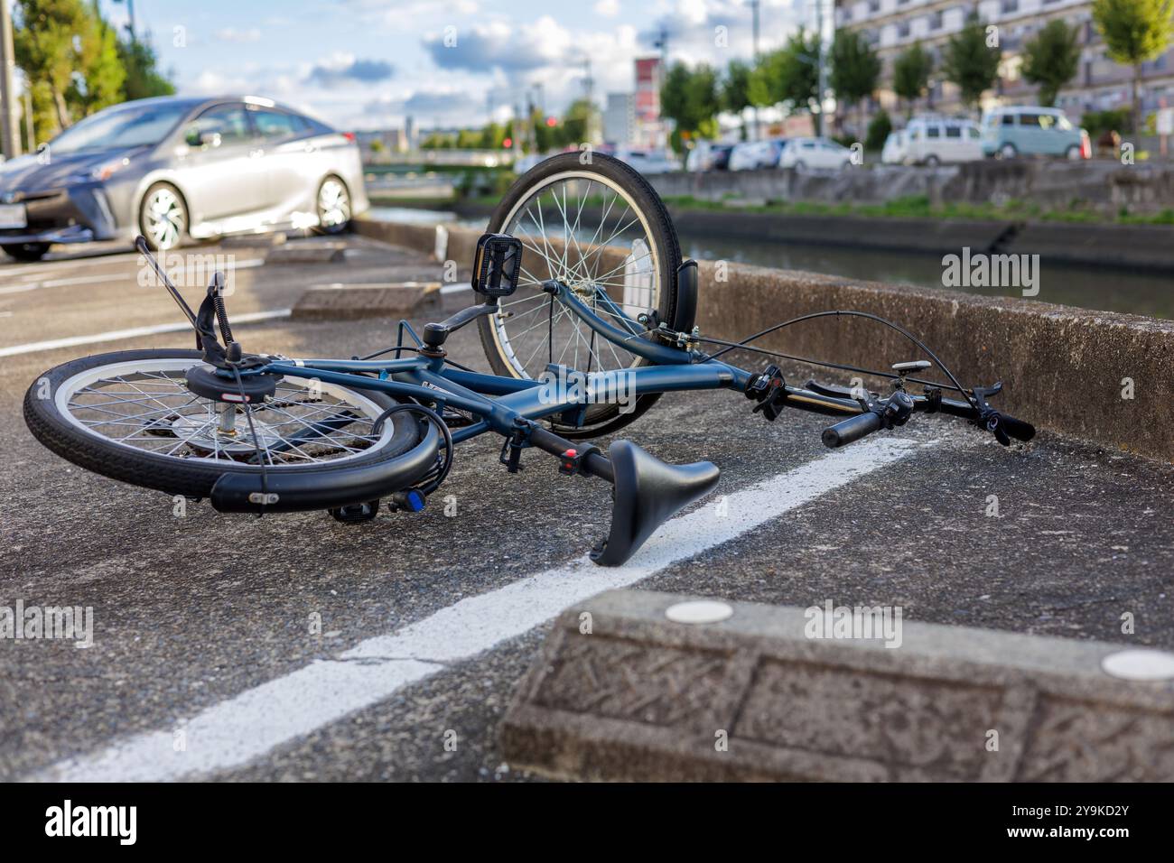 A bicycle lies on its side in a parking lot next to a row of cars. The ...
