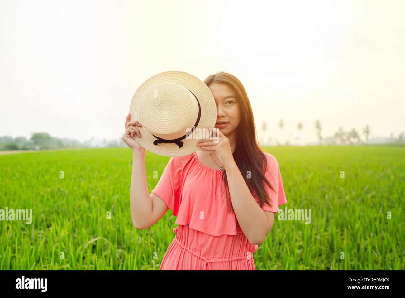 A beautiful Asian girl is holding a rattan hat with covering her left ...