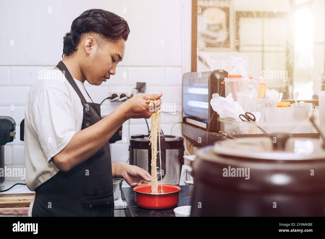A Southeast Asian chef with an apron is stirring the noodles in the red ...