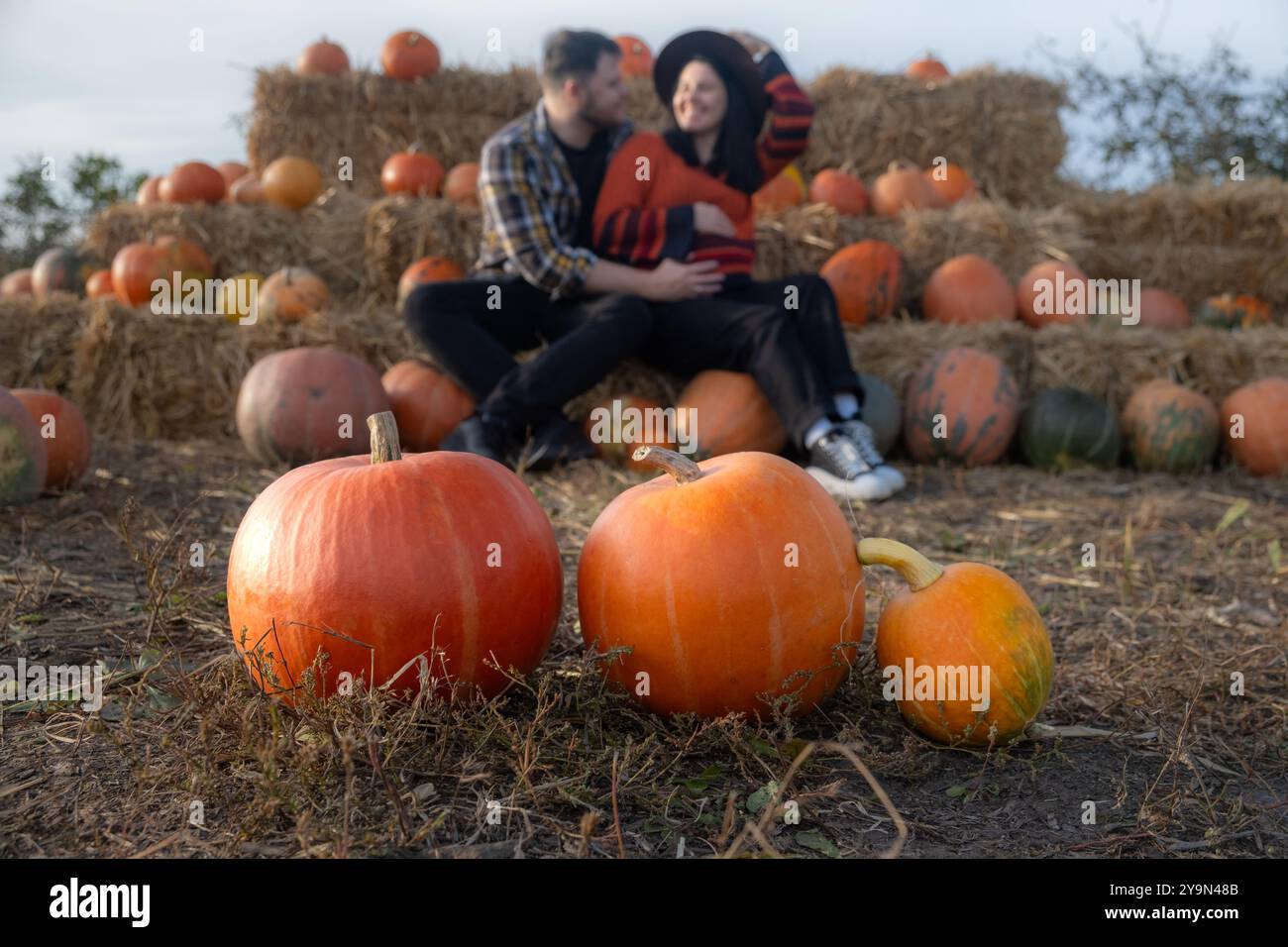 Couple sitting on hay bales in a pumpkin patch Stock Photo - Alamy