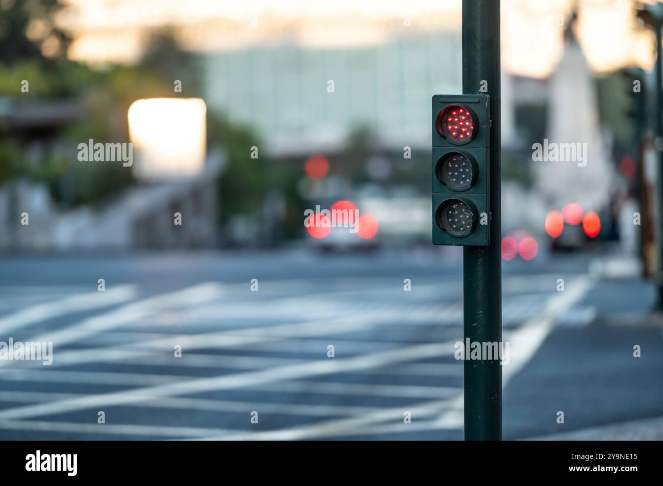A red traffic signal stands at a busy urban intersection as cars pass ...