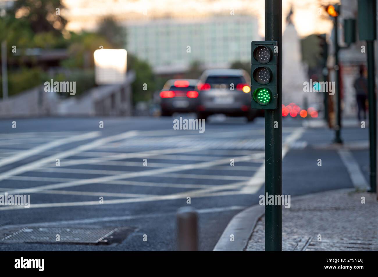 A green traffic signal stands at a busy urban intersection as cars pass ...