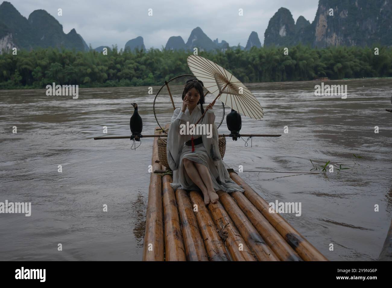 Hanfu girl seated on a bamboo raft holds an umbrella while fixing her ...