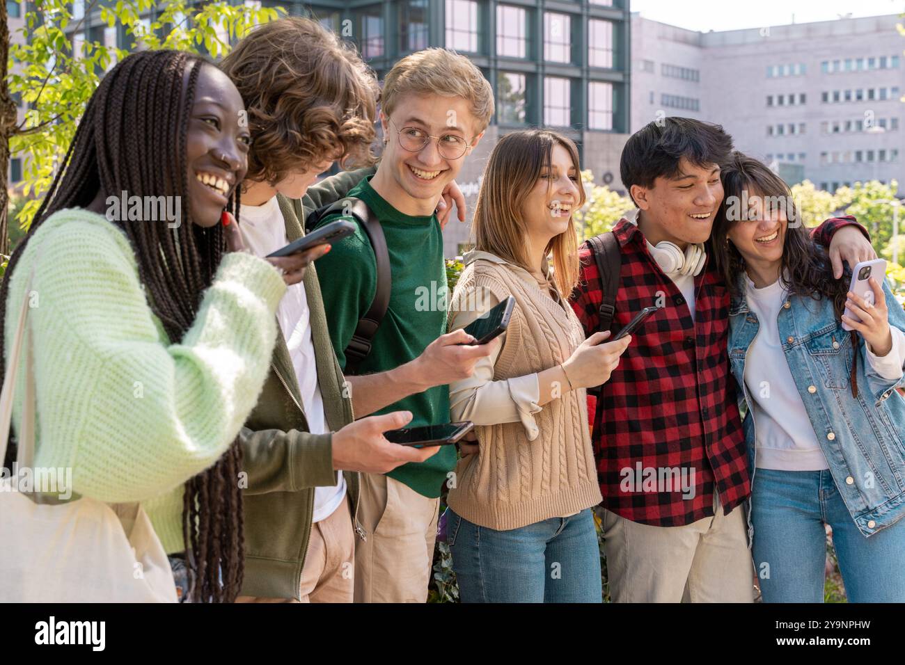 Group of diverse young students smiling and using smartphones together ...