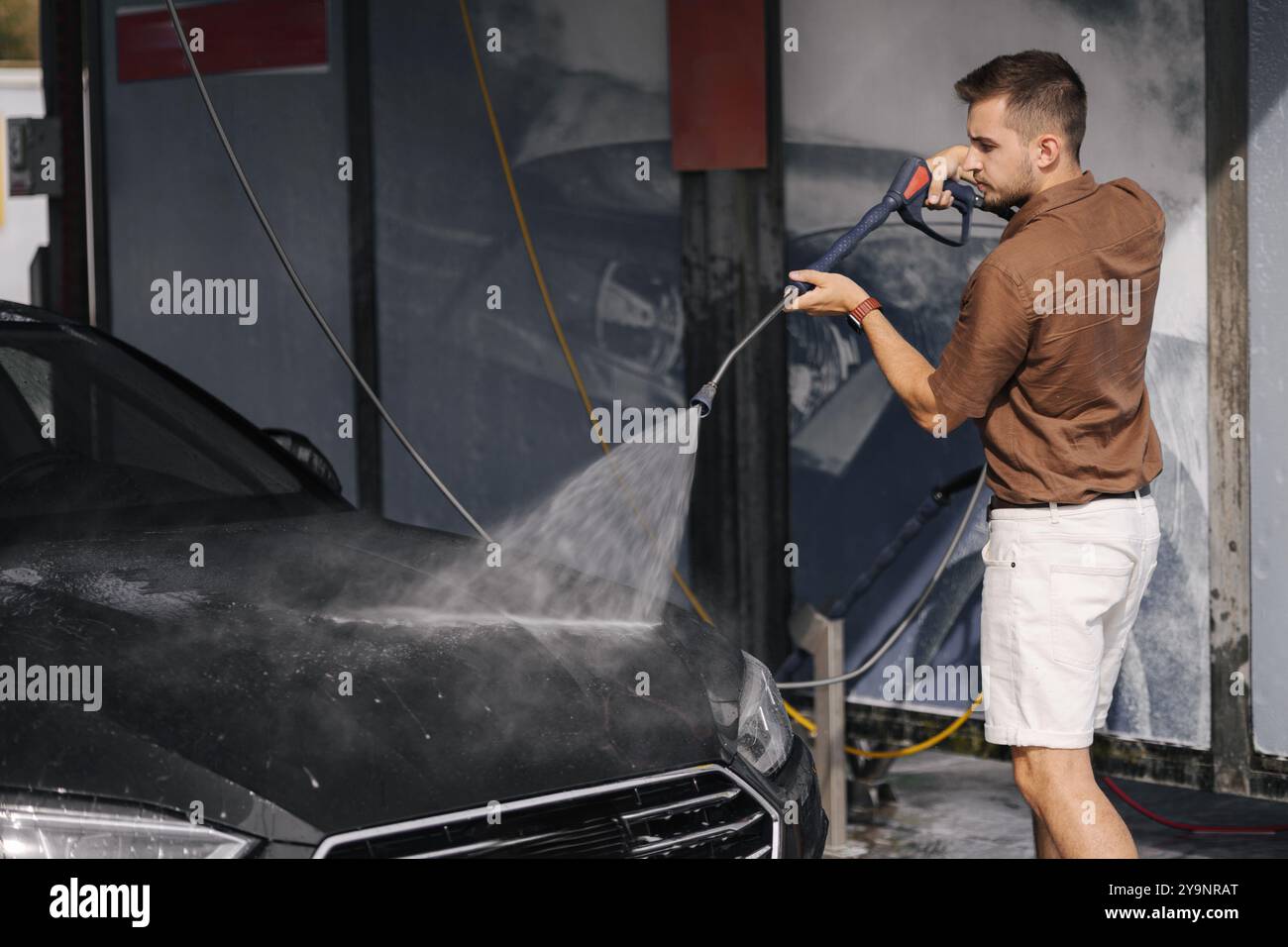 Side view of young man cleaning his car with a jet sprayer. Self ...