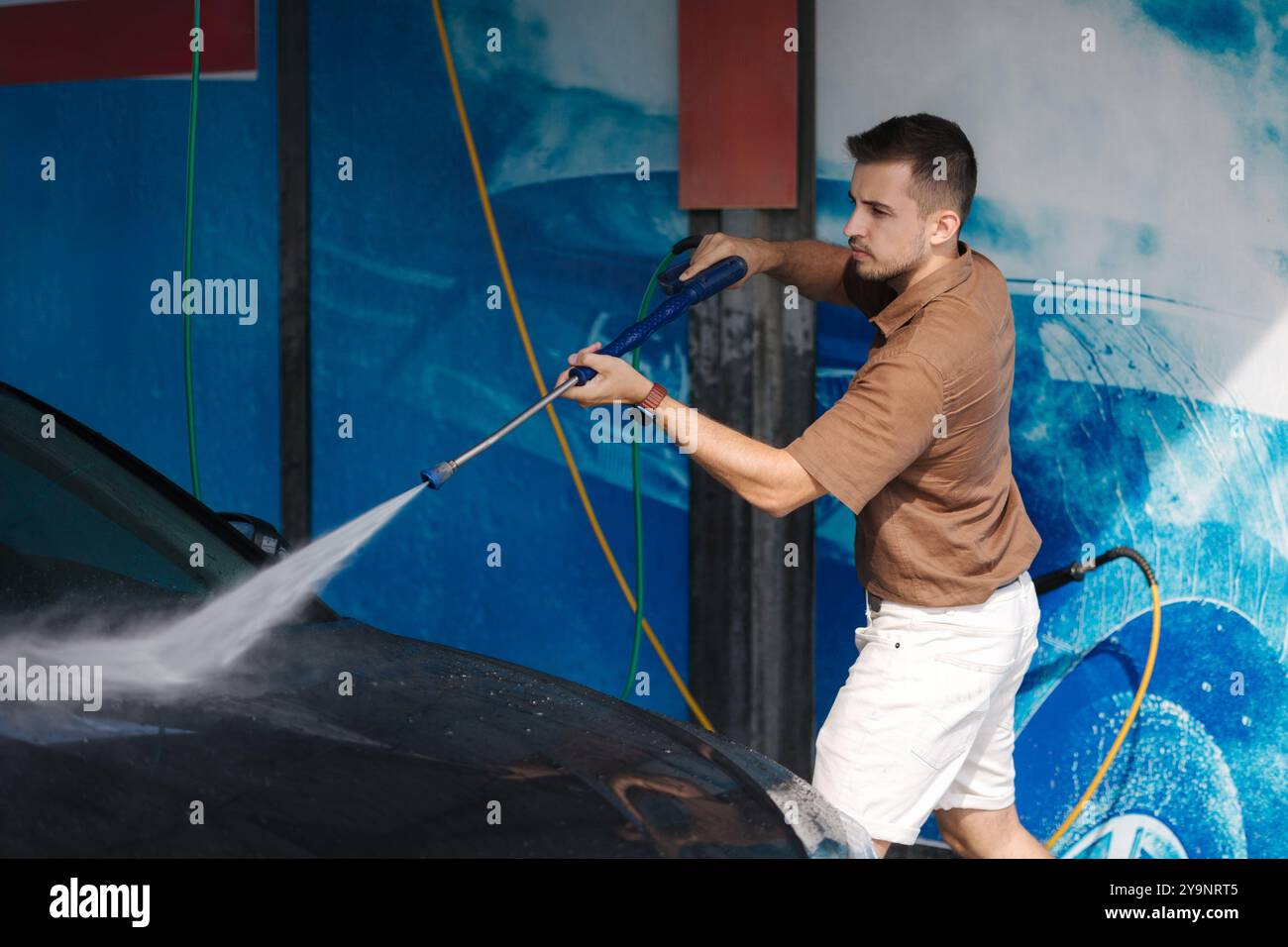 Side view of young man cleaning his car with a jet sprayer. Self ...