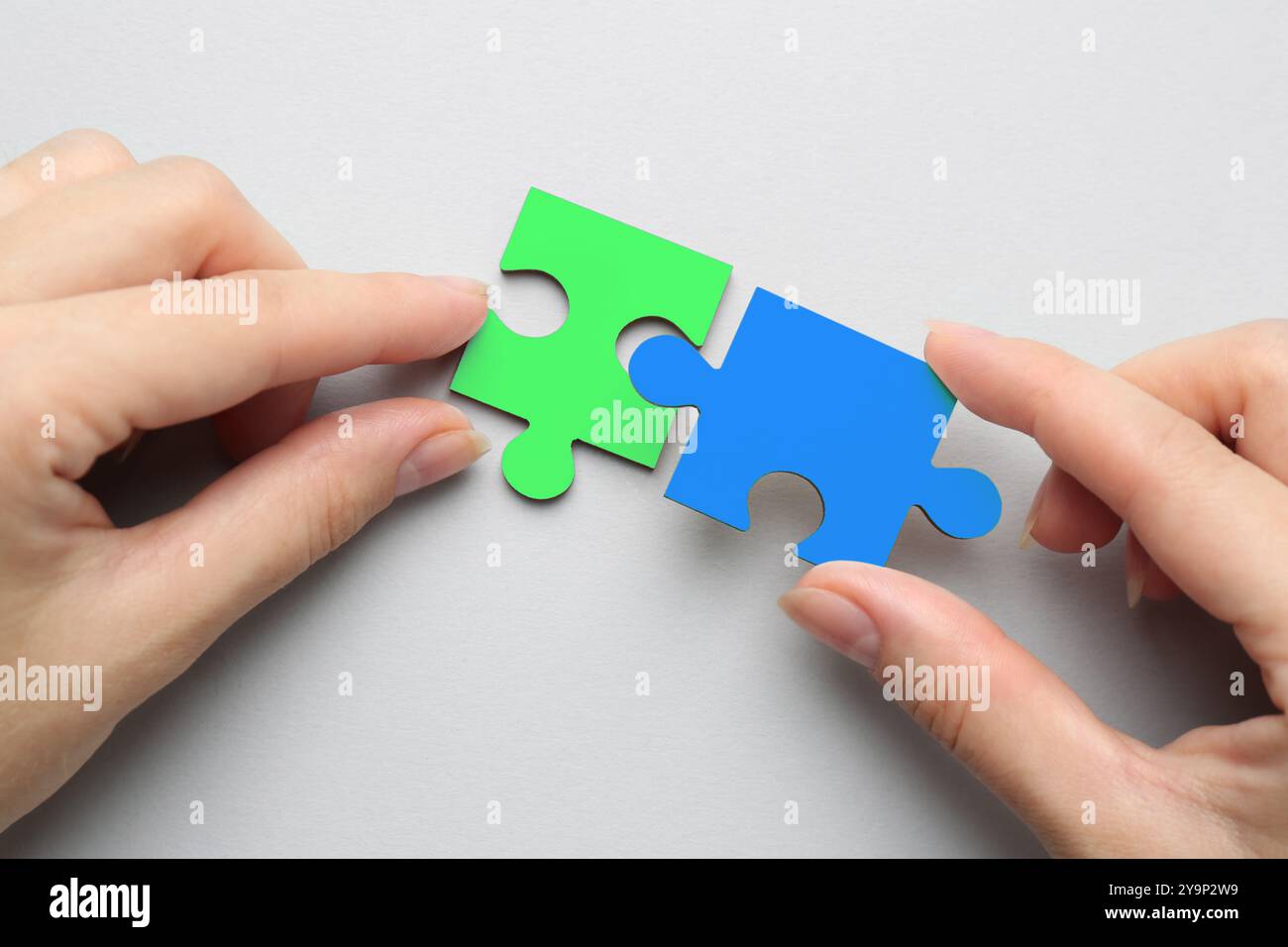 Woman joining puzzle pieces on light grey background, top view. Autism ...