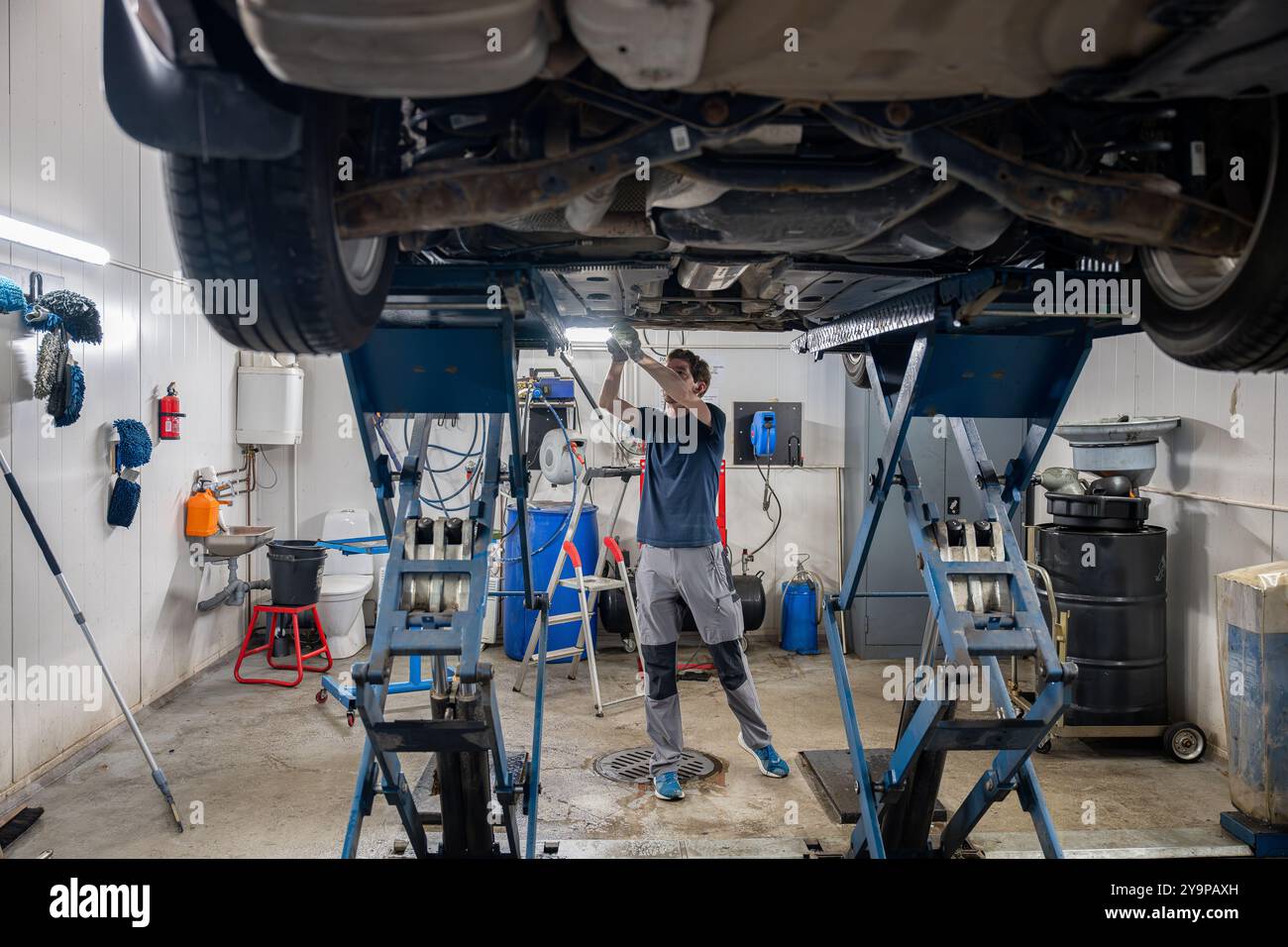 car mechanic standing under lifted car and fixing car in garage Stock ...
