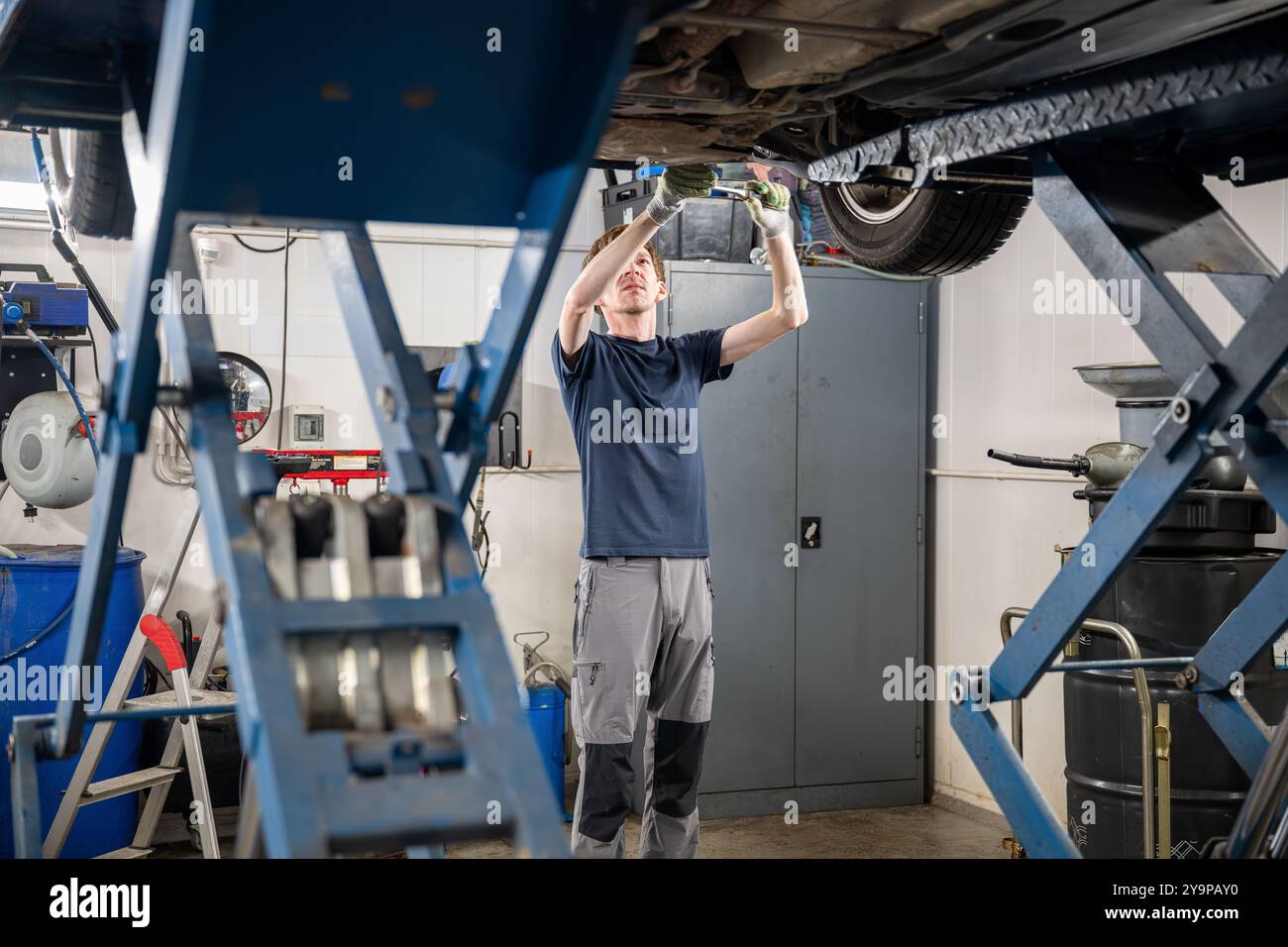 car mechanic standing under lifted car and fixing car in garage Stock ...