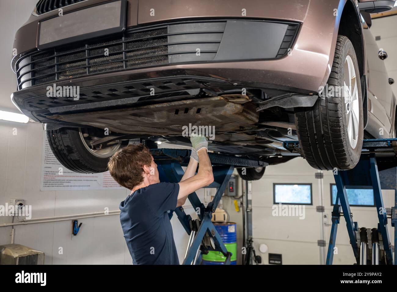 car mechanic standing under lifted car and fixing car in garage Stock ...