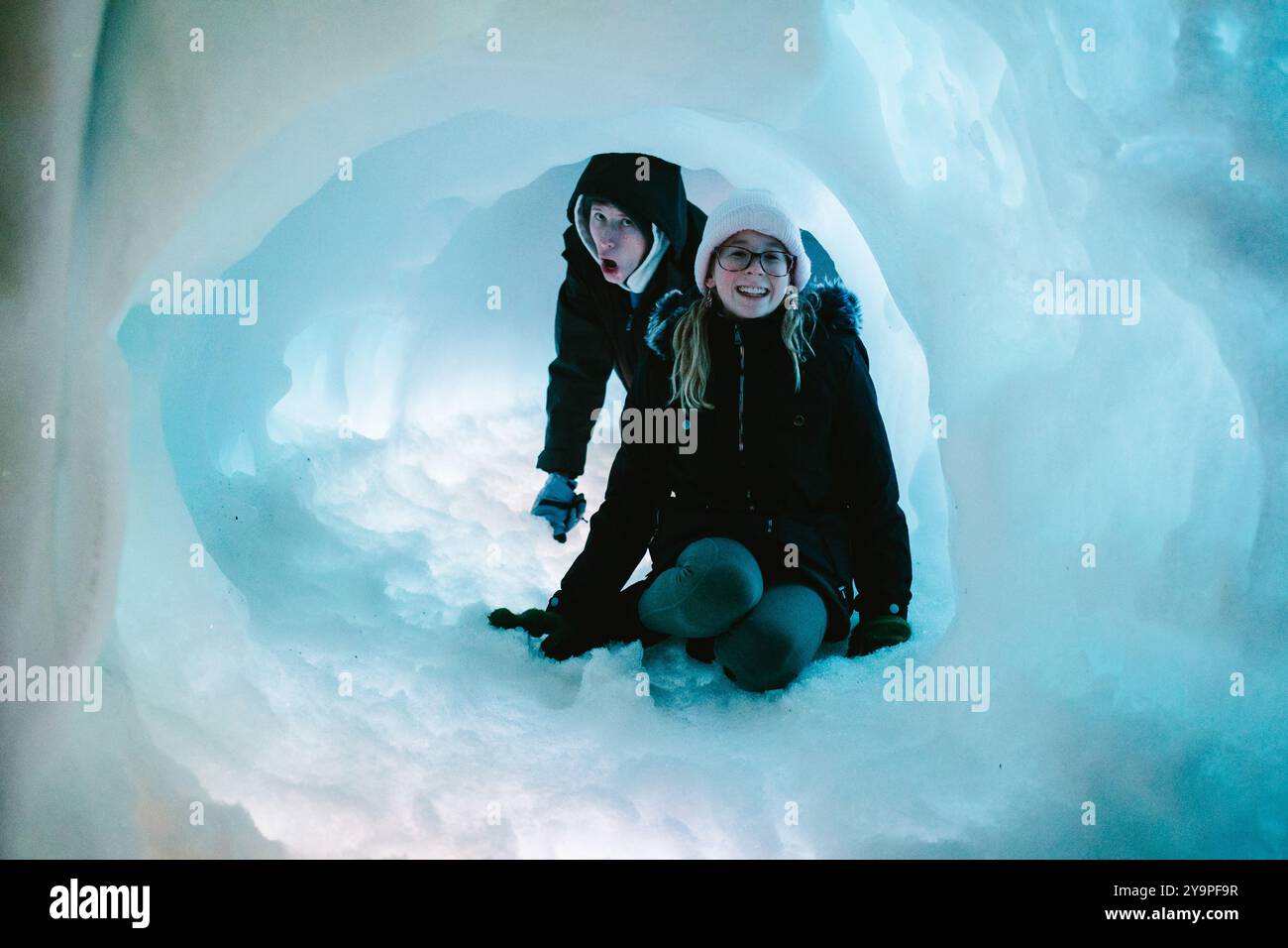 Sister and brother climb through snow tunnel in ice cave Stock Photo ...