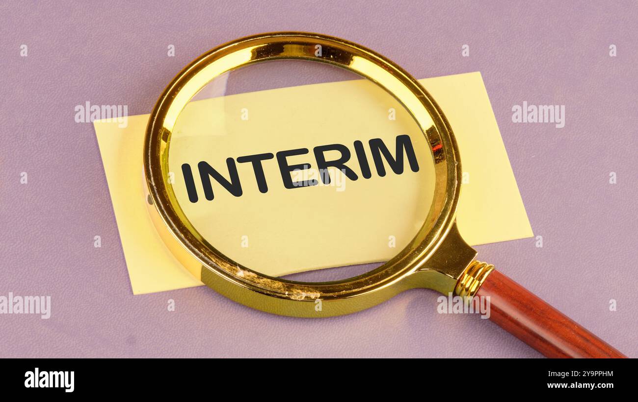 A word INTERIM on a yellow business card through a magnifying glass ...