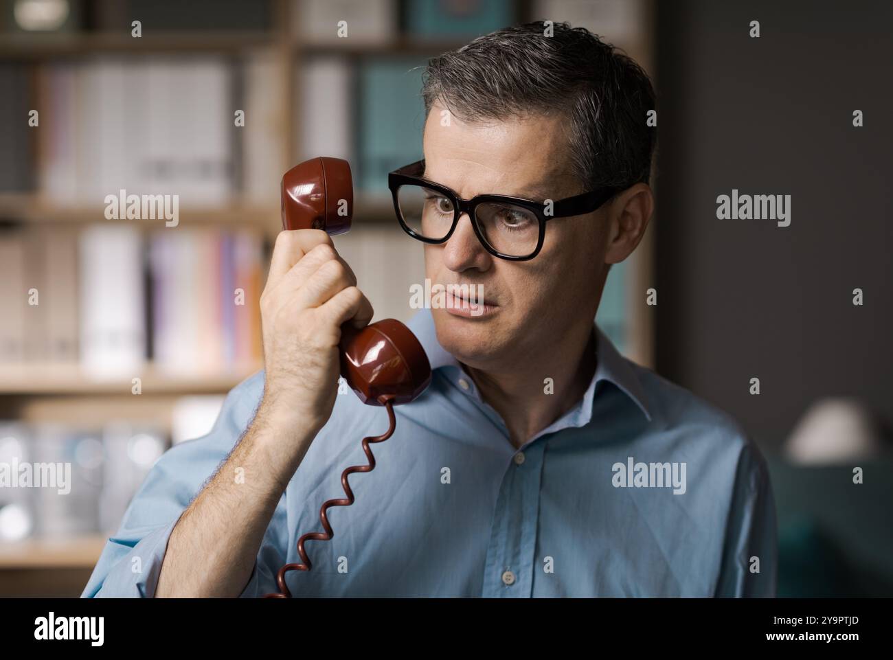 Shocked office worker staring at the phone receiver, he is confused and ...