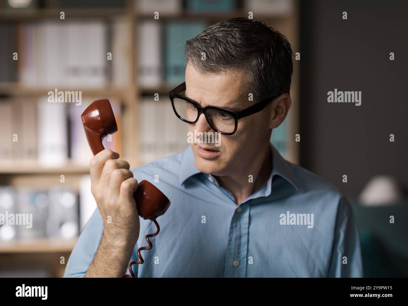 Shocked office worker staring at the phone receiver, he is confused and ...