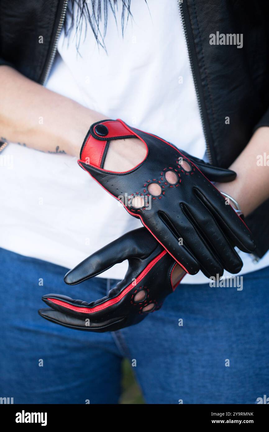 A woman in a black leather jacket wearing black driving gloves with red ...