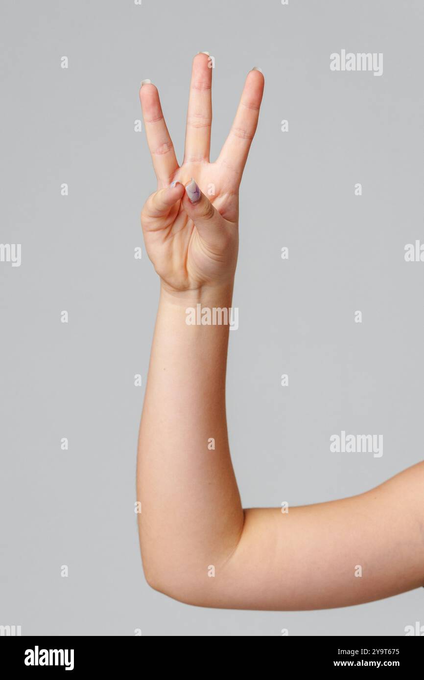 A hand showing the number three with fingers raised against a light ...