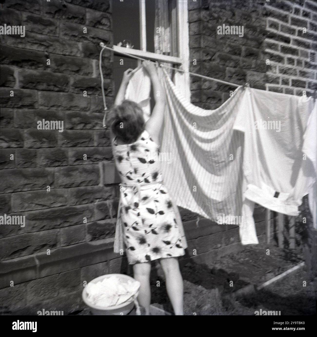 1950s, historical, outside a stone-built terraced house, a lady putting ...