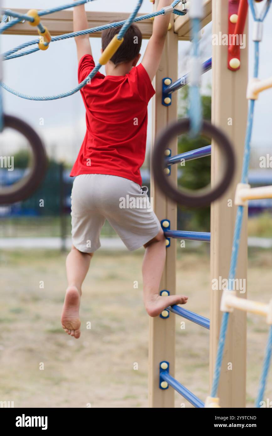 Happy boy playing and hanging on rings on playground. Kids exercises ...