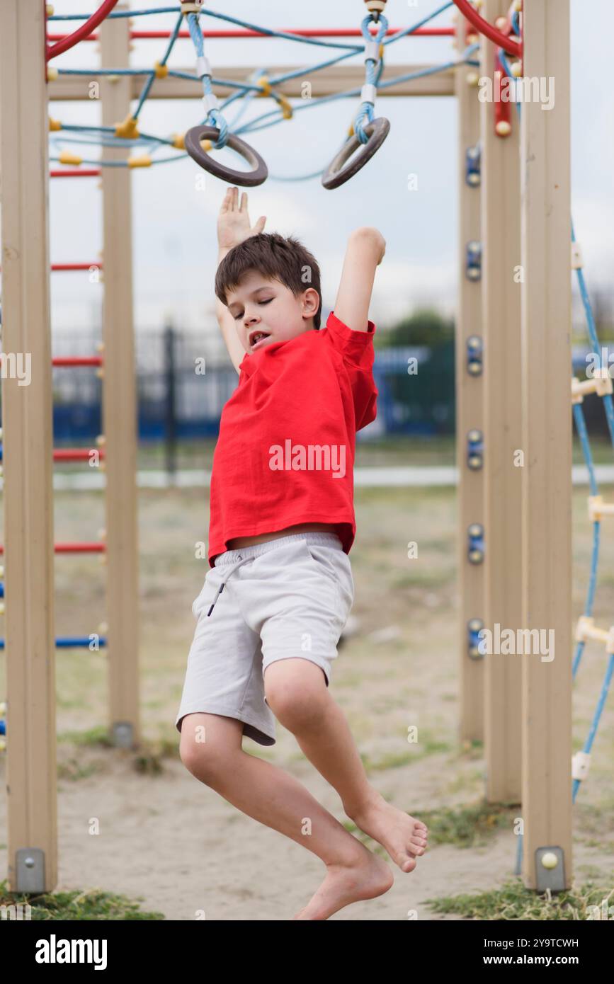 Happy boy playing and hanging on rings on playground. Kids exercises ...