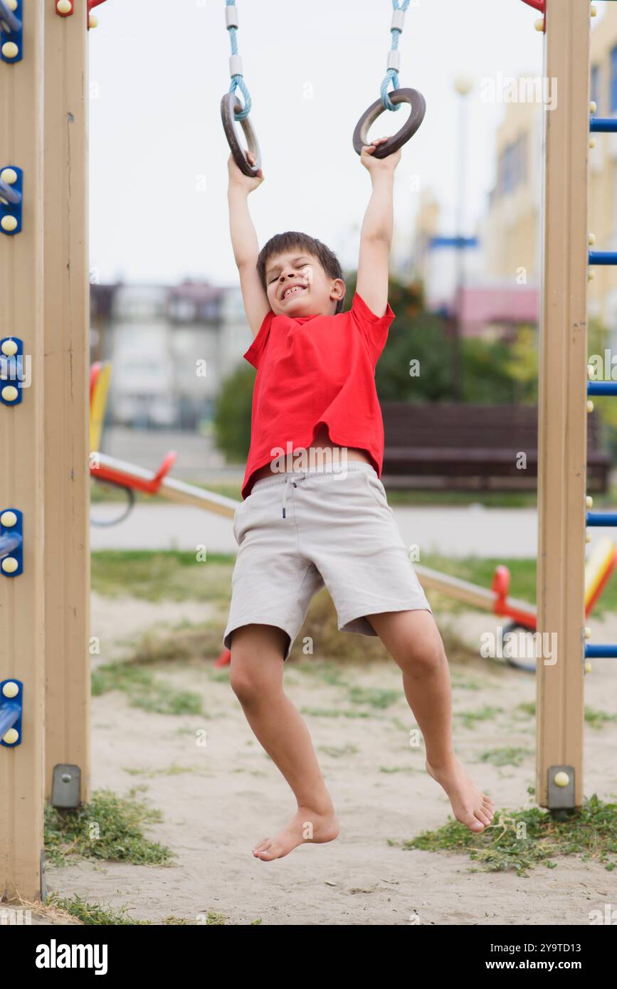 Happy boy playing and hanging on rings on playground. Kids exercises ...