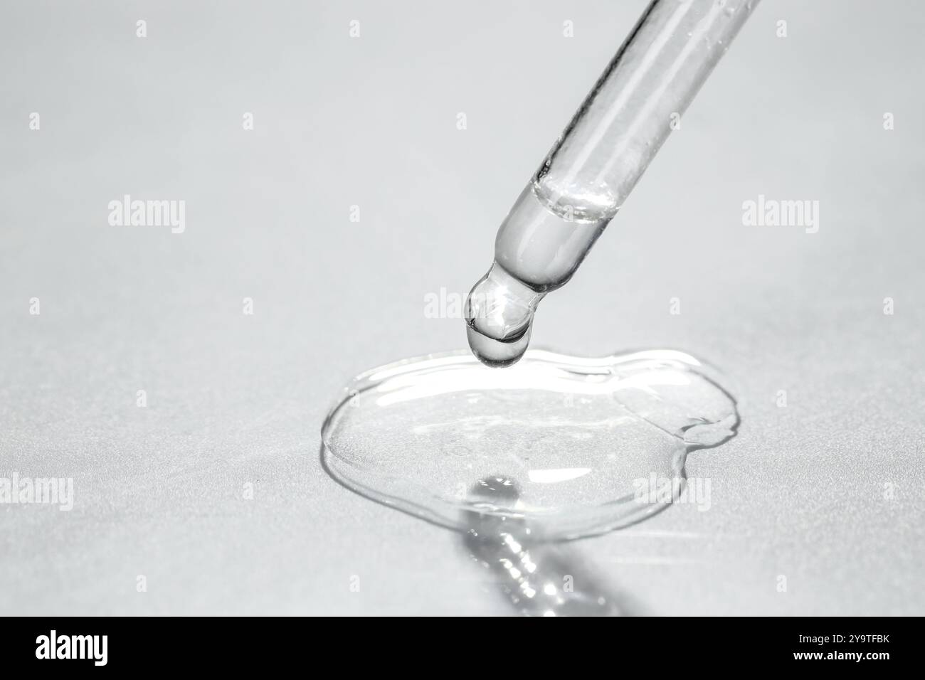 Cosmetic oil dripping from pipette on light grey background, closeup ...