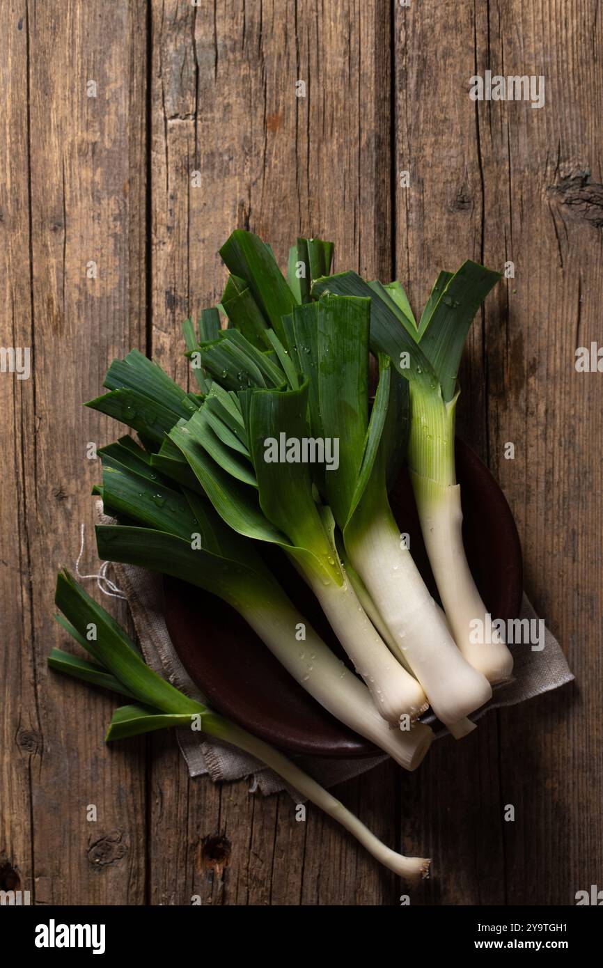 A bunch of green leeks in a brown bowl on a wooden table. Photo in a ...
