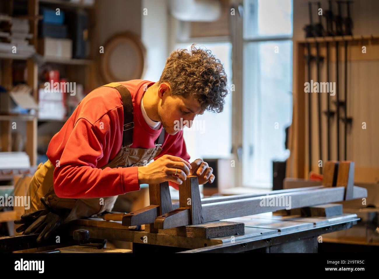 Focused woodworker applies leather pads to bed legs in workshop ...