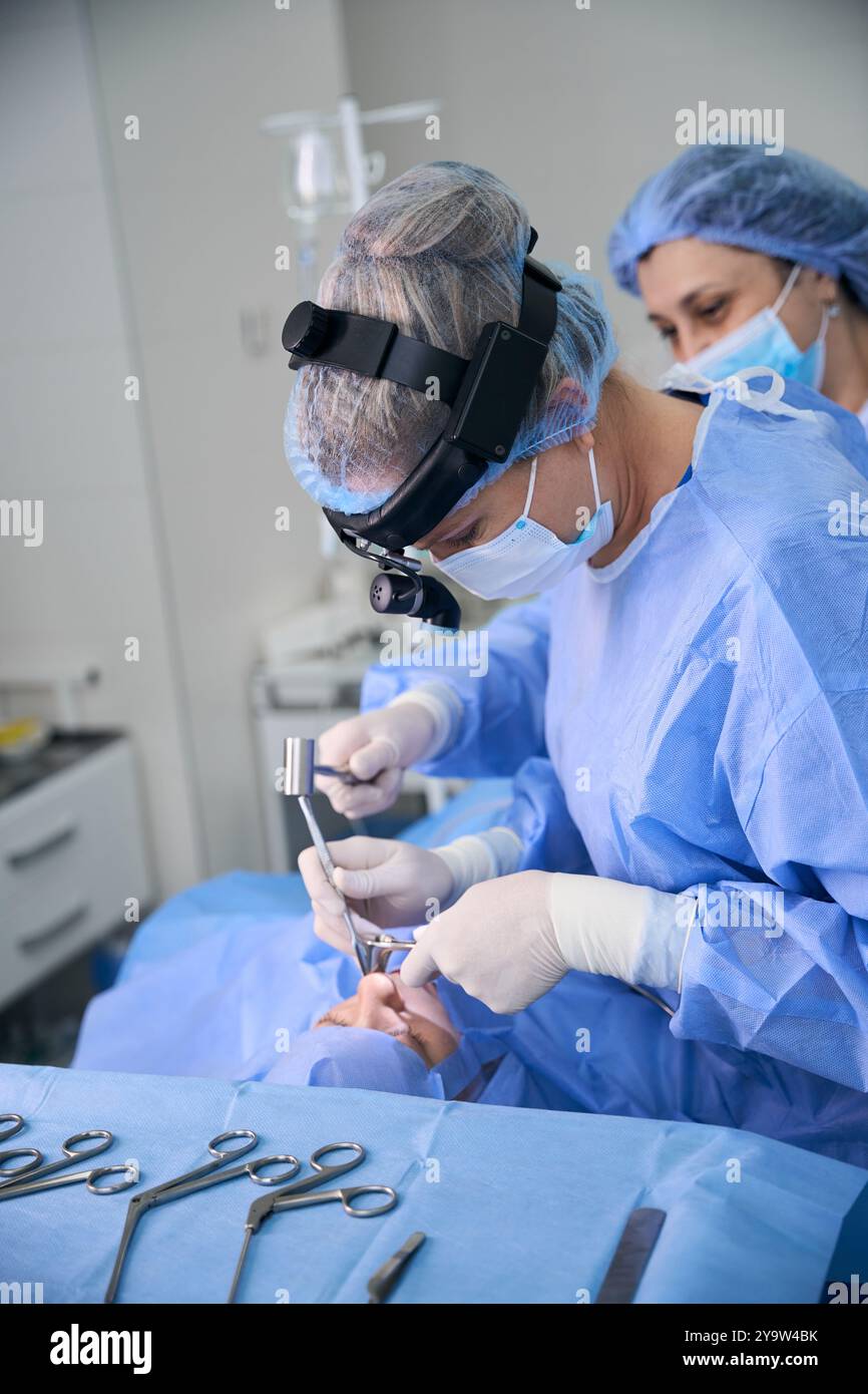 Female surgeon uses a surgical headlamp while working, with a patient ...