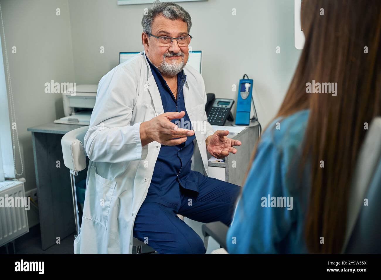 Adult doctor explaining procedure to seated patient Stock Photo - Alamy