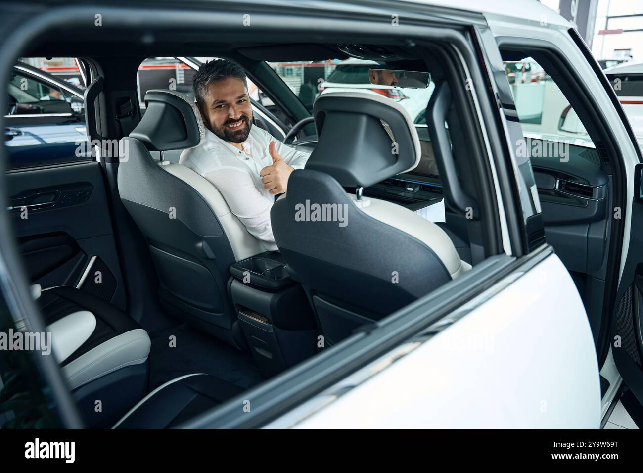 Happy man checking new luxury car, showing thumbs up in dealership ...