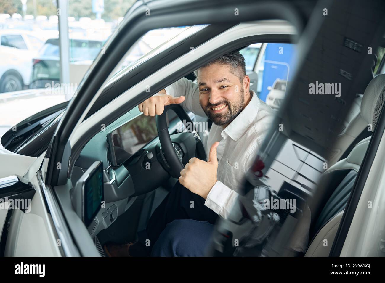 Smiling man checking new car, showing thumbs up in dealership center ...