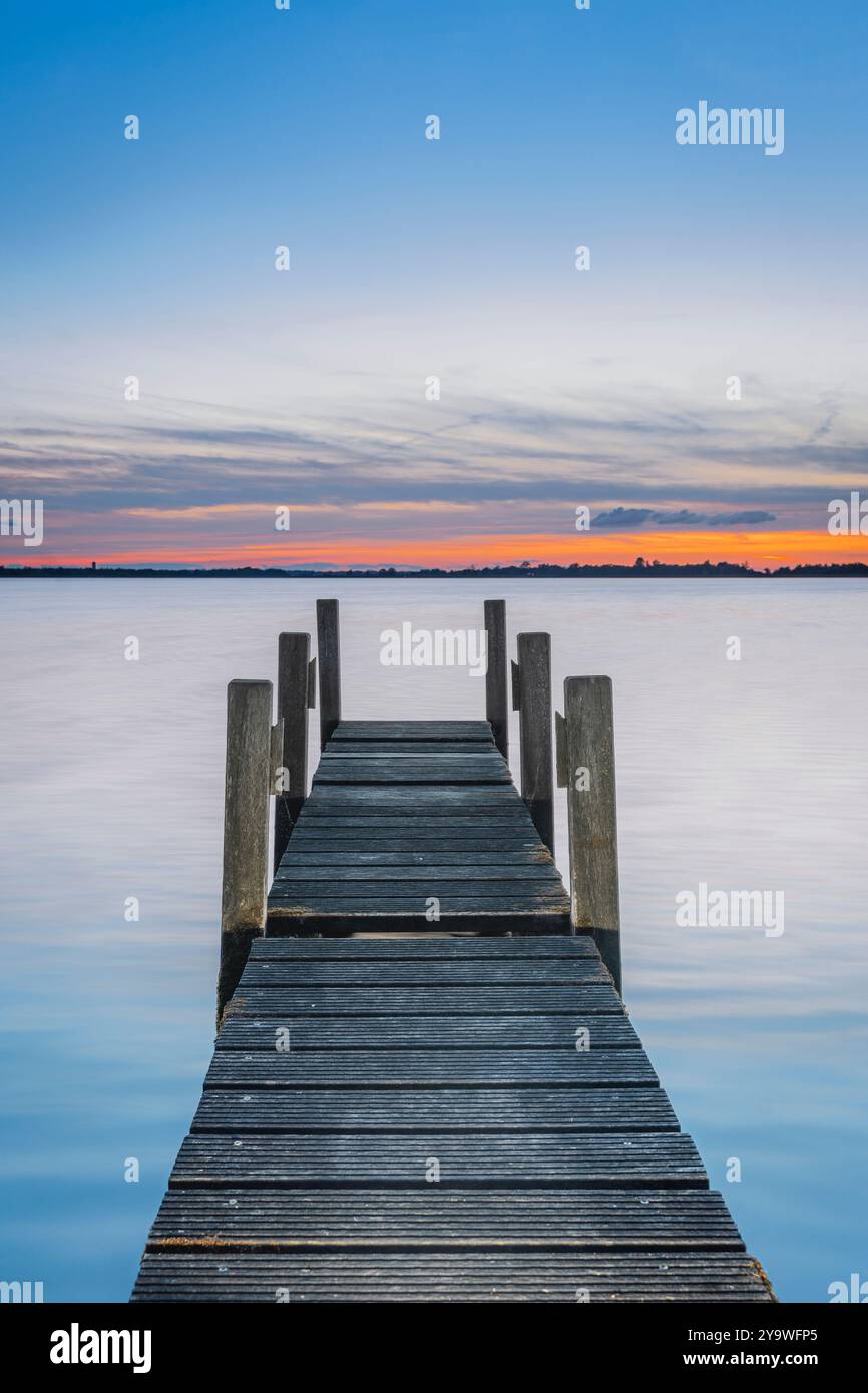 Water and lake with wooden jetty (pier) with the setting sun on the ...