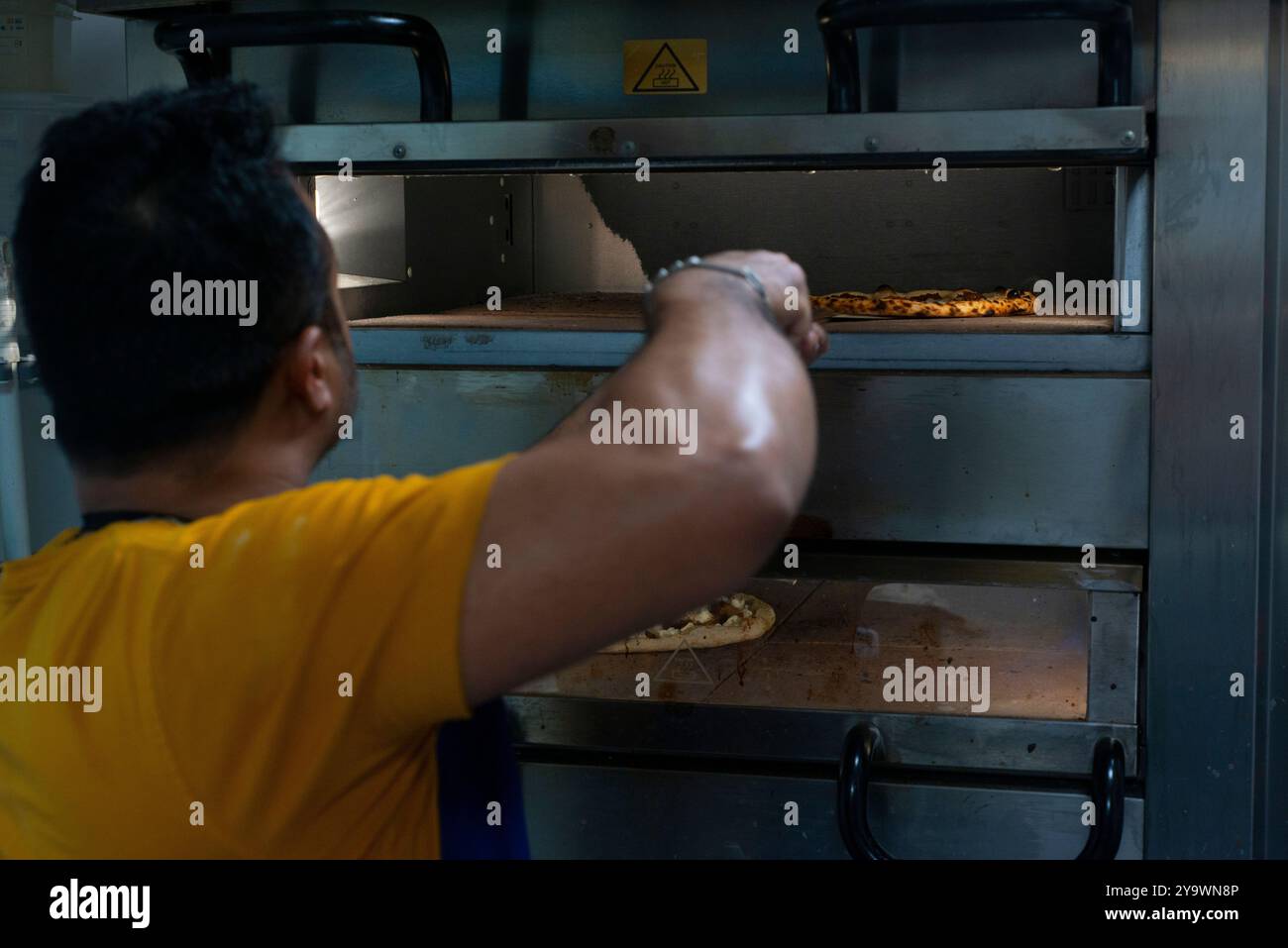 Kitchen helper putting pizza in the oven Stock Photo - Alamy