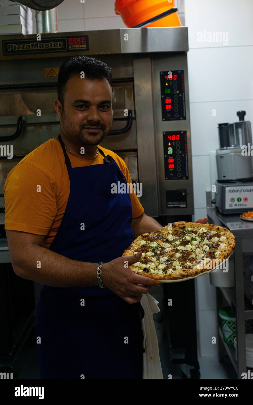 Kitchen assistant showing a pizza fresh out of the oven Stock Photo - Alamy