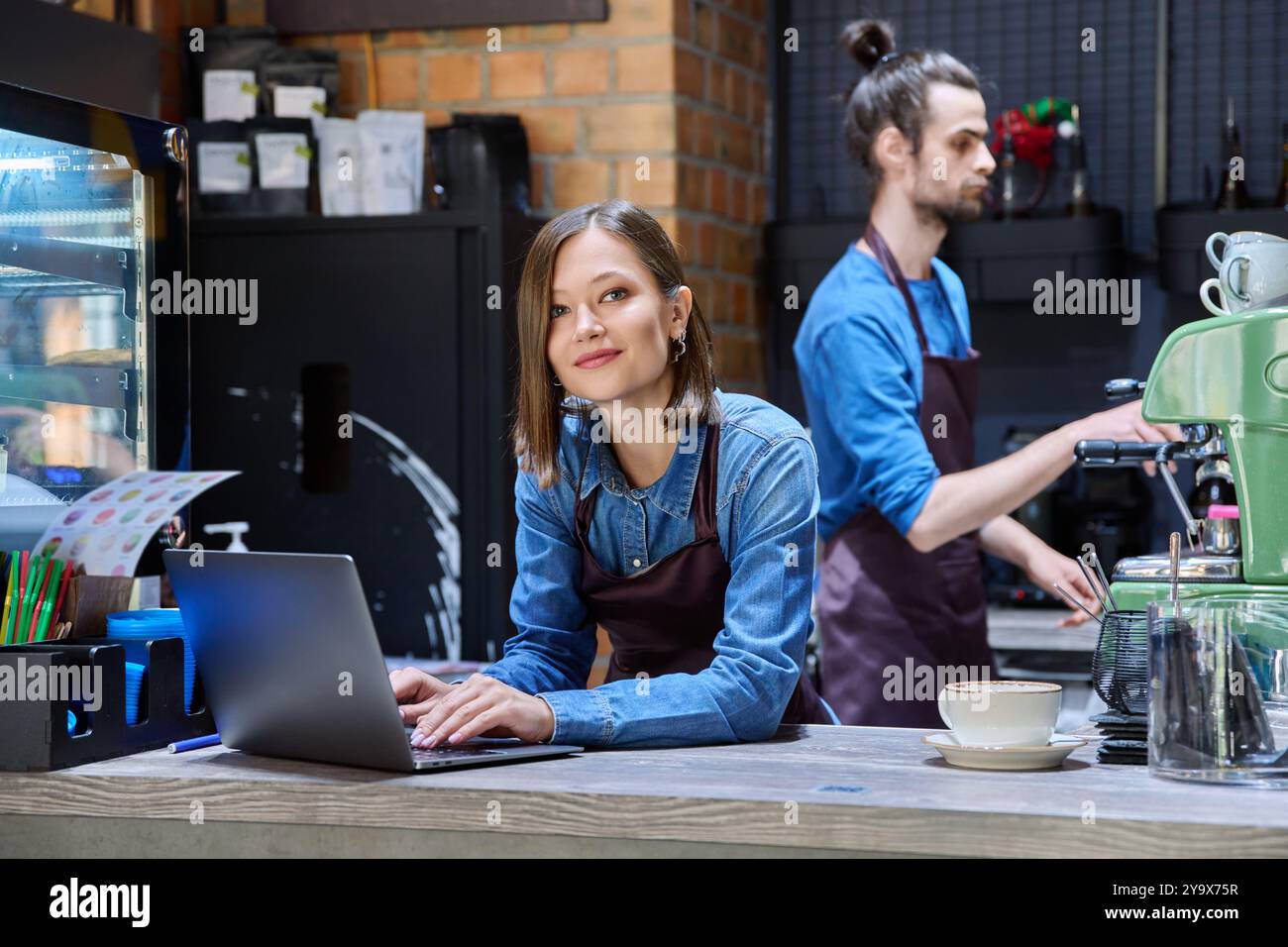 Young woman coffee shop worker in apron using laptop computer at bar ...
