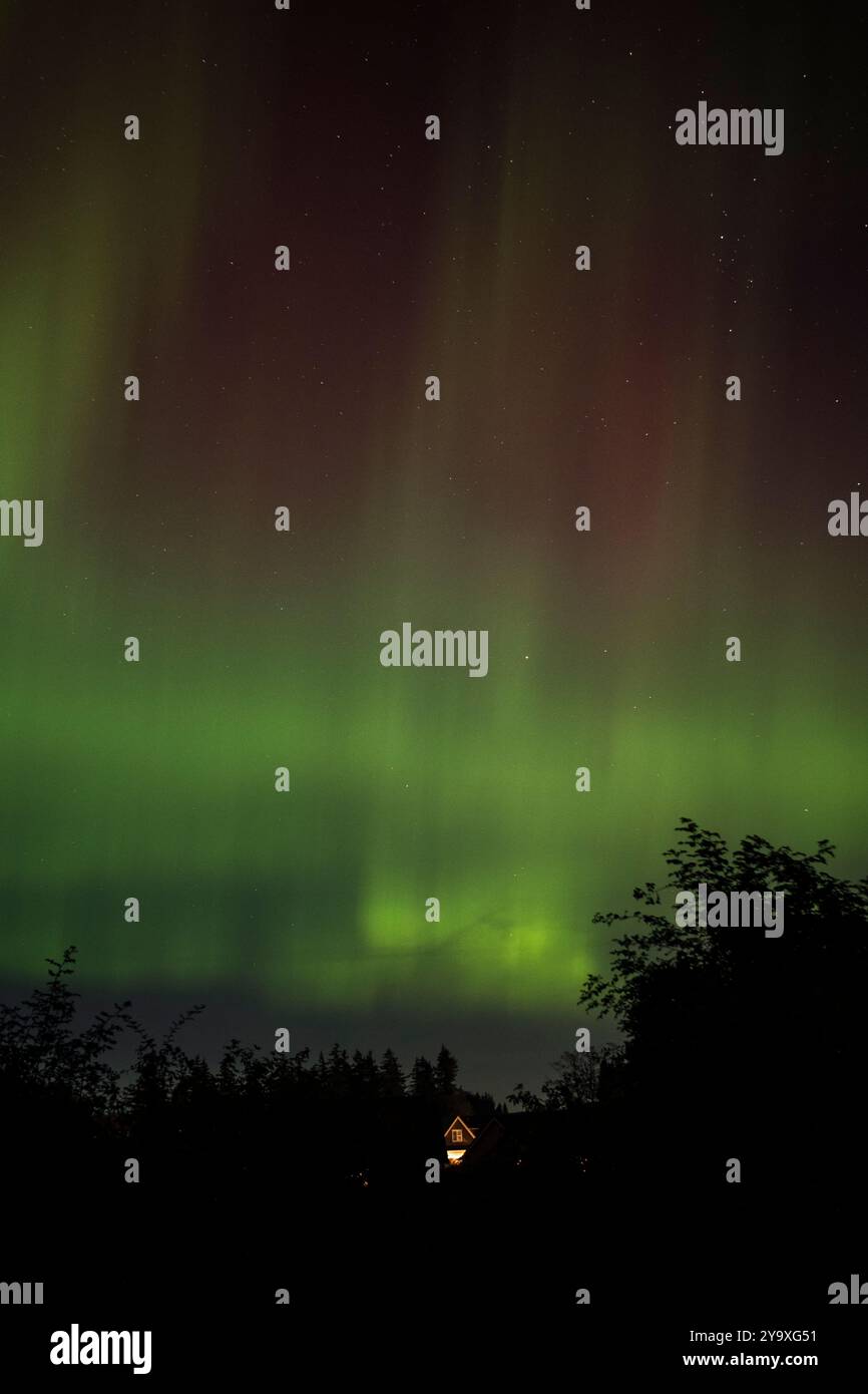 Northern Lights seen over a small house lit up at night in the woods ...