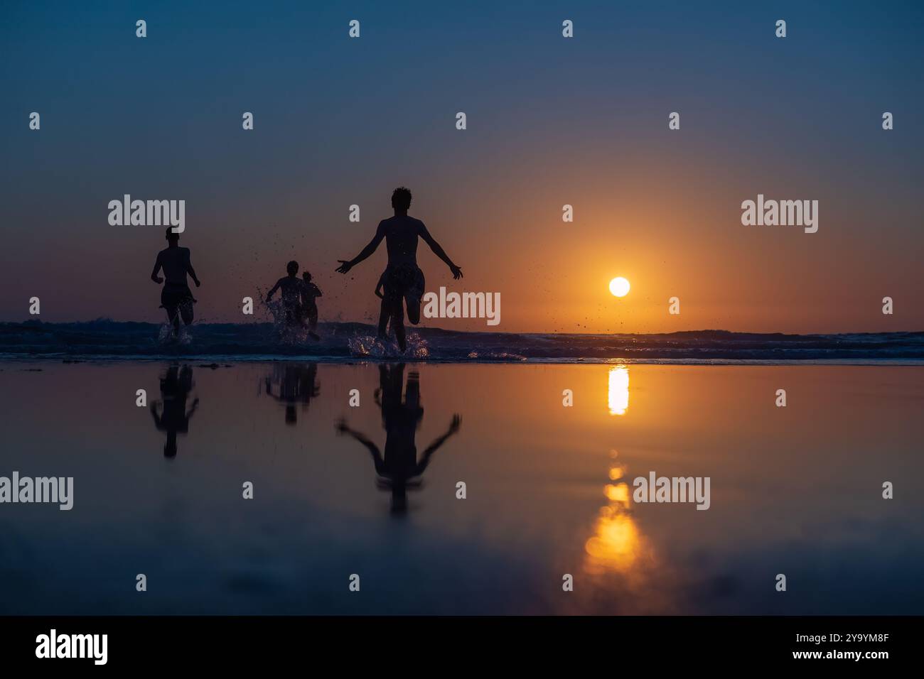 Silhouettes of people running on a beach during sunset, with their ...