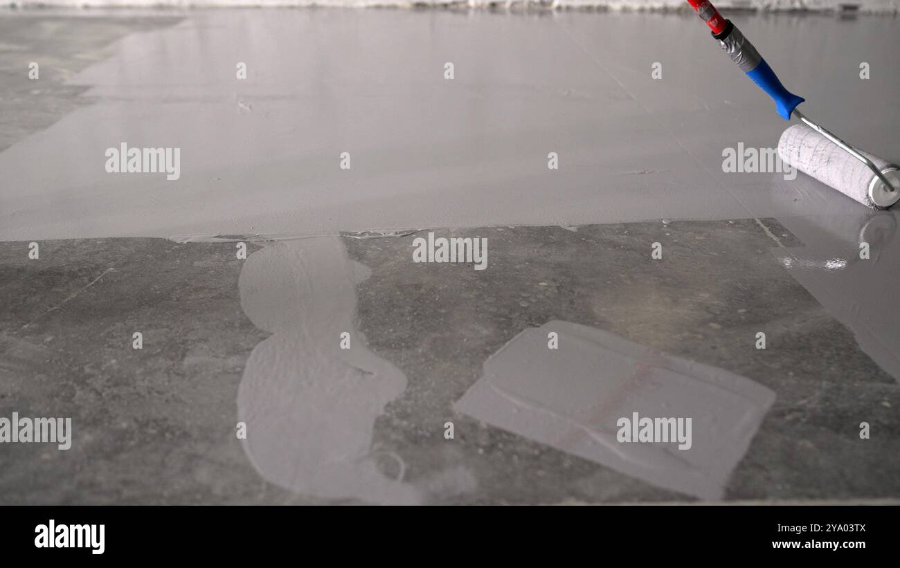 Construction worker is applying epoxy coating on a concrete floor using ...
