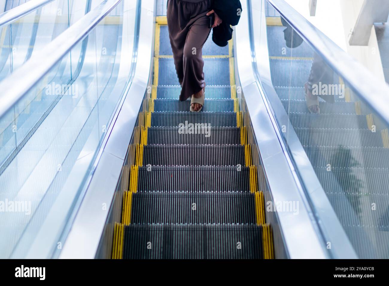 A person walking up an escalator, wearing a long brown skirt and ...