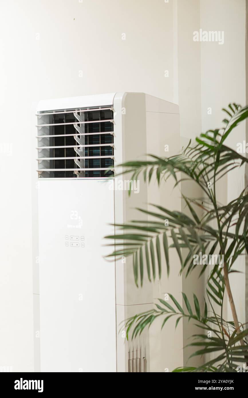 A modern white air conditioning unit positioned next to a green indoor ...