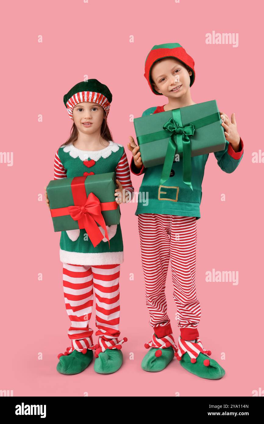 Cute little children in elf's costumes with gift boxes on pink ...