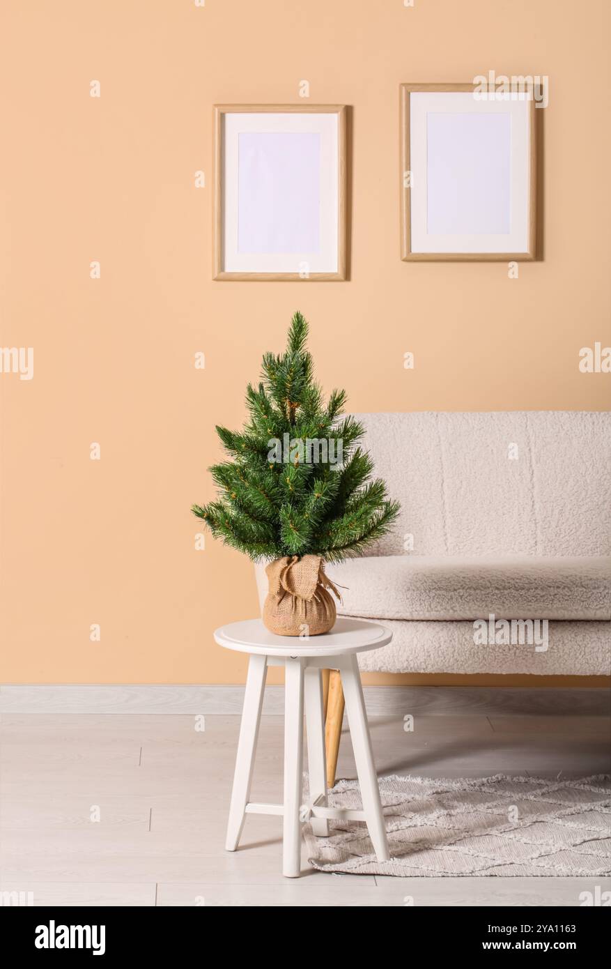 Small Christmas tree on stool with sofa near beige wall Stock Photo - Alamy
