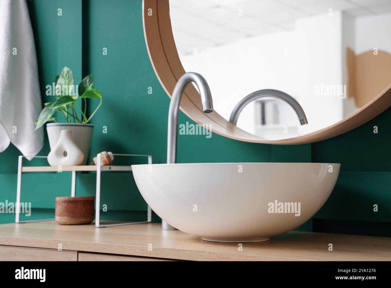 Modern sink, vase and houseplant on chest of drawers near green wall in ...