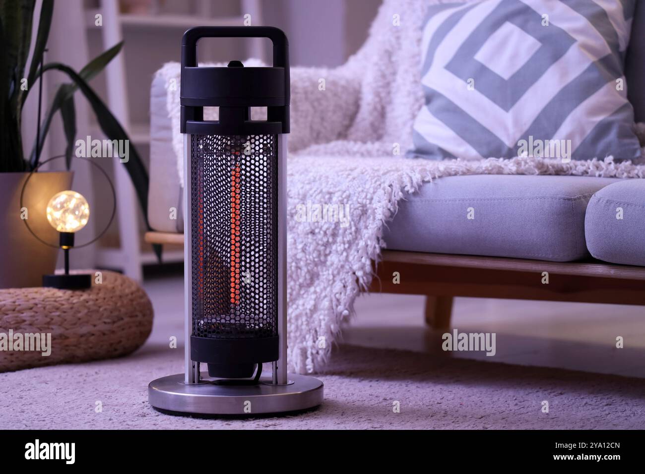 Stylish sofa with modern electric heater in room at evening Stock Photo ...