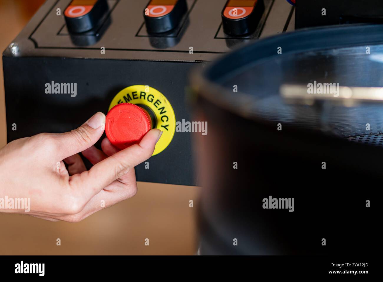 A close-up of a hand reaching for a red emergency stop button on a ...