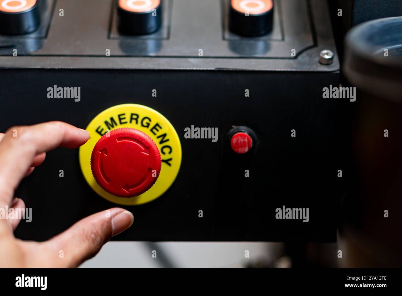 A close-up of a hand reaching for a large red emergency stop button on ...