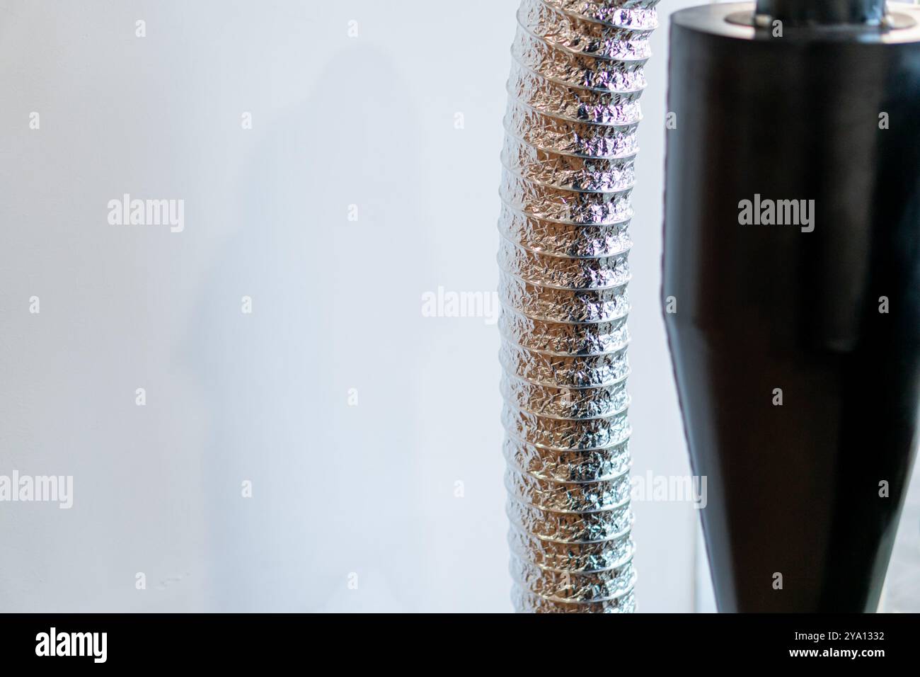 A close-up view of a metallic flexible ducting hose next to a black ...