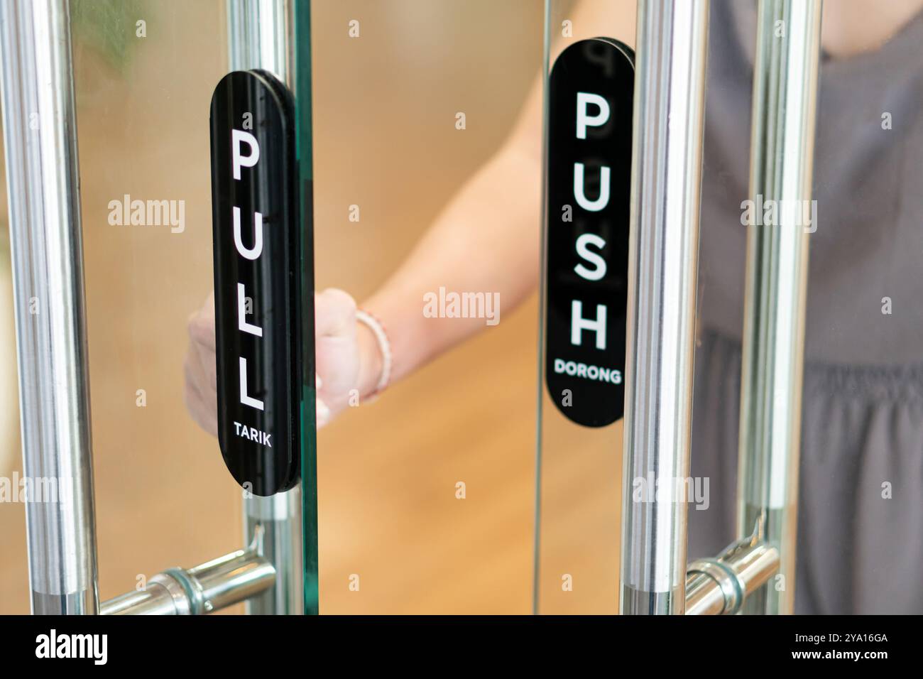 A person is interacting with a glass door that has clear signage ...